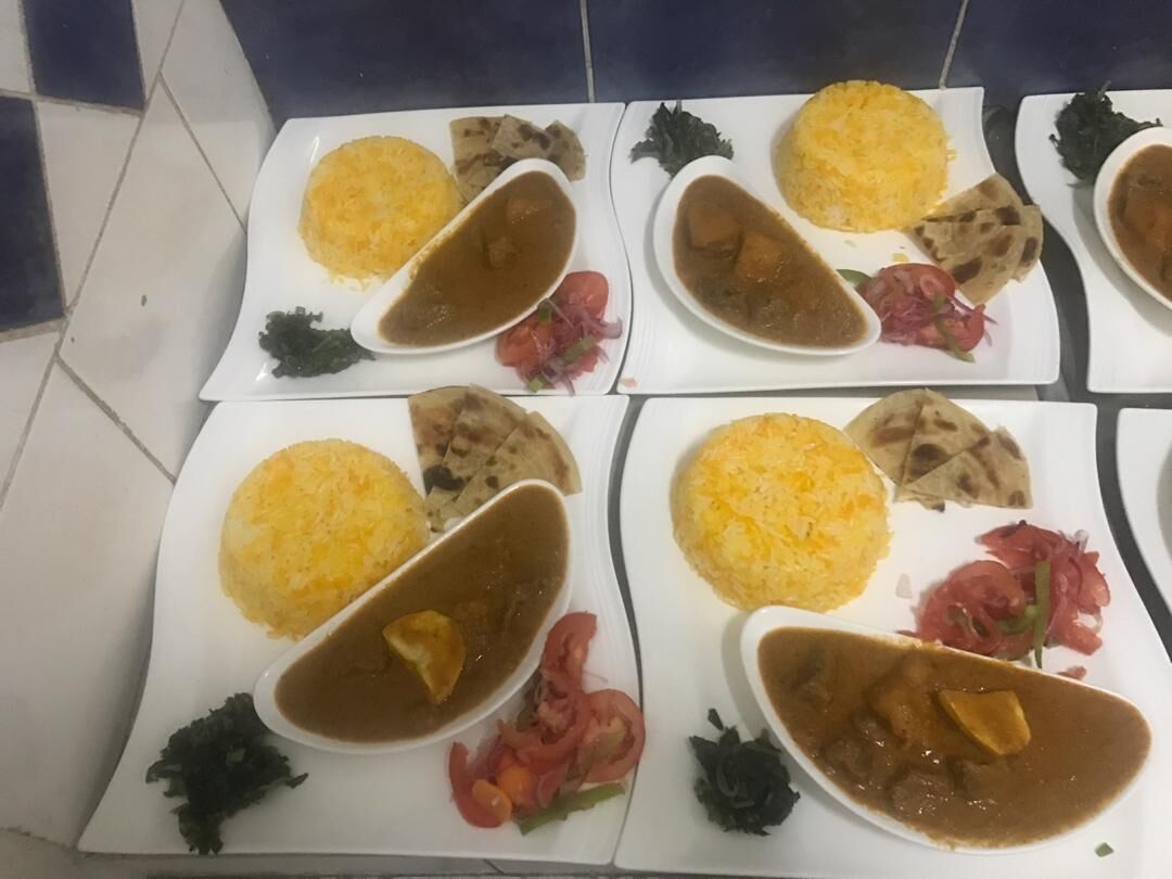 Uma mesa com vários pratos de comida, cada um contendo arroz, um prato de carne, pão achatado e um acompanhamento de legumes.