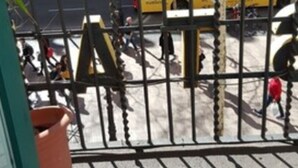 Uma varanda com vista para a rua, um grade de metal e um vaso de planta.