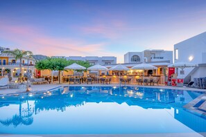 Área de piscina com espreguiçadeiras e guarda-sóis, um bar e vista para os edifícios ao redor.