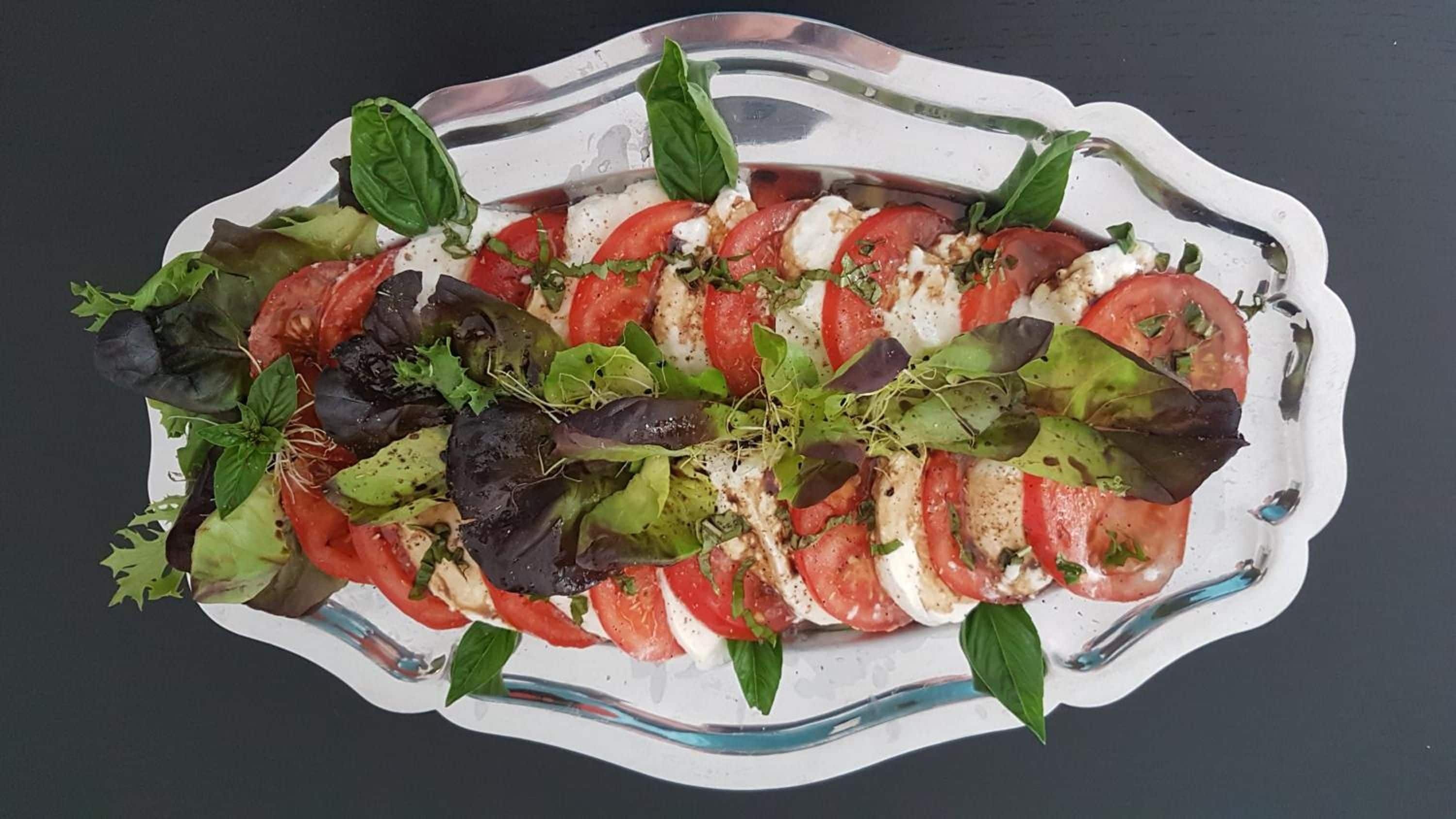 Uma salada Caprese com tomates, mussarela e manjericão em um prato branco.