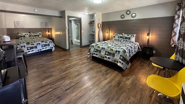 Quarto de hotel com duas camas, uma escrivaninha, uma cadeira e uma mesinha.
