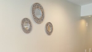Um quarto com duas poltronas azuis com capitonê, uma pequena mesa preta e três espelhos decorativos na parede.