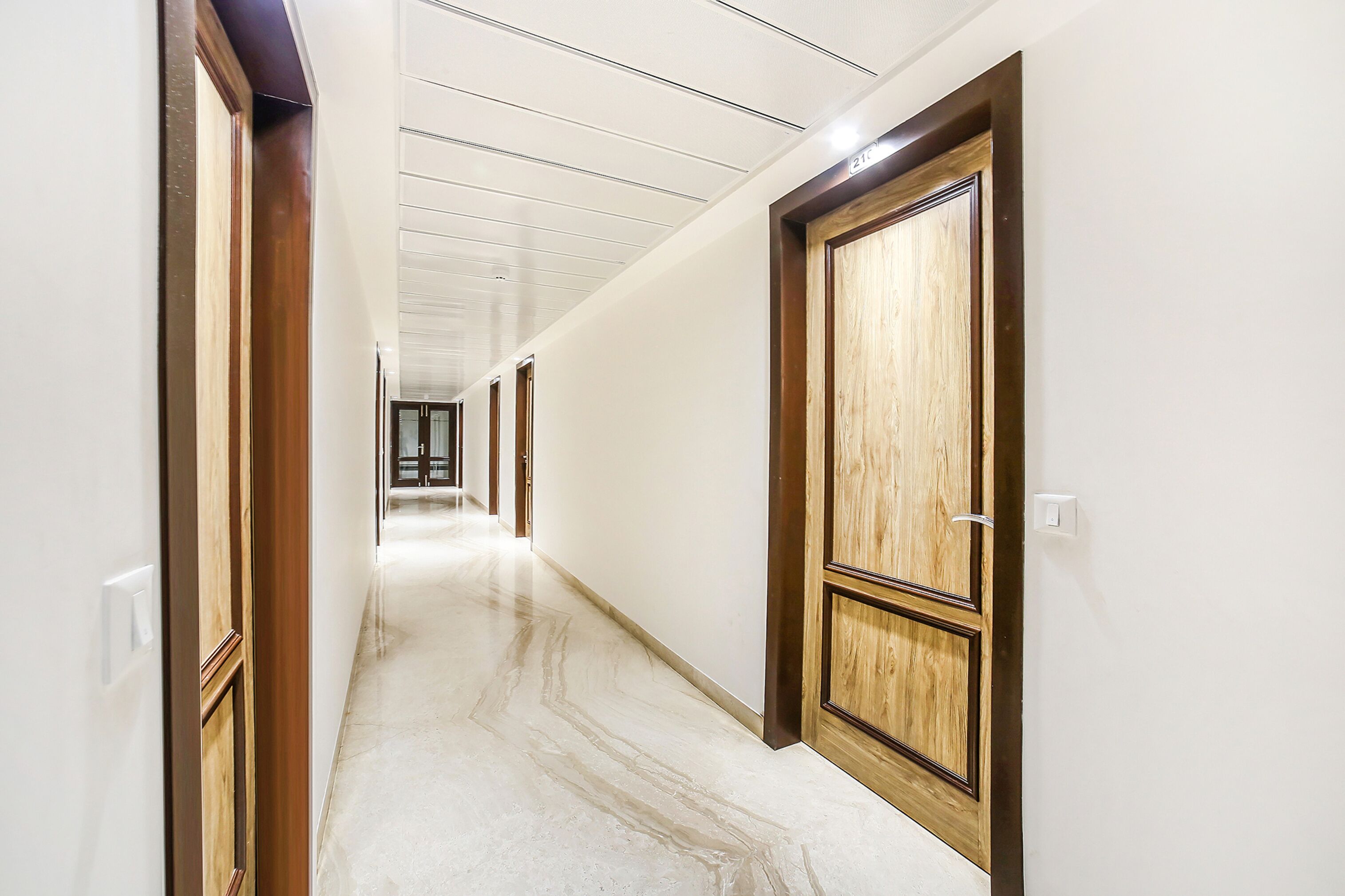 Um corredor com portas de madeira e paredes brancas, que leva a um quarto com vista.