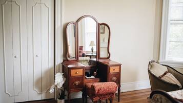 Quarto com toucador de madeira, espelho, um banquinho pequeno e uma cadeira.
