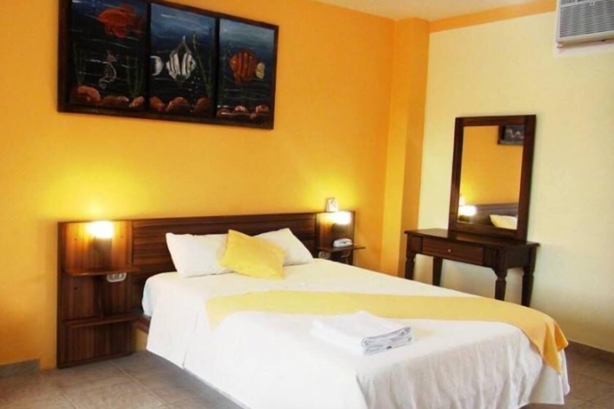 Quarto de hotel com uma cama grande, duas luminárias de cabeceira, mesa de apoio, uma cadeira e um quadro acima da cama.