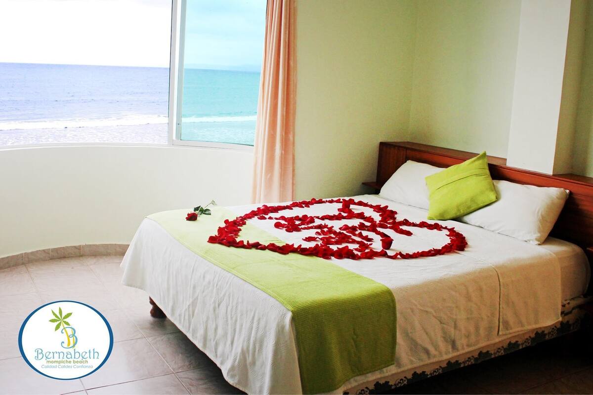 Quarto de hotel com uma cama, vista para a praia e um logotipo na parede.