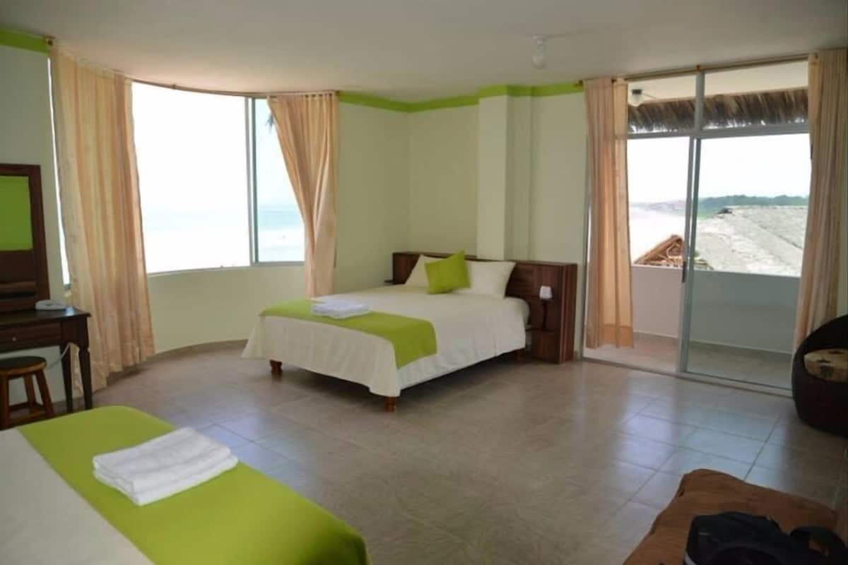 Quarto de hotel com cama, escrivaninha e vista para a praia.