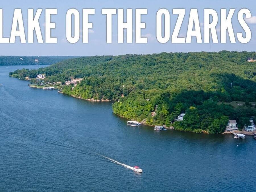 Um lago com barcos, rodeado por colinas arborizadas e casas.