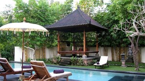 Uma área de piscina com espreguiçadeiras, um gazebo e vegetação exuberante.