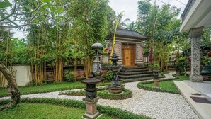 Um pátio tradicional com lanternas de pedra, um pequeno pagode e vegetação exuberante.