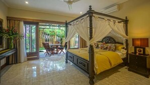 Uma cama de dossel com cortina, um ventilador de teto, uma mesa de cabeceira e vista para um jardim através de uma porta de vidro.