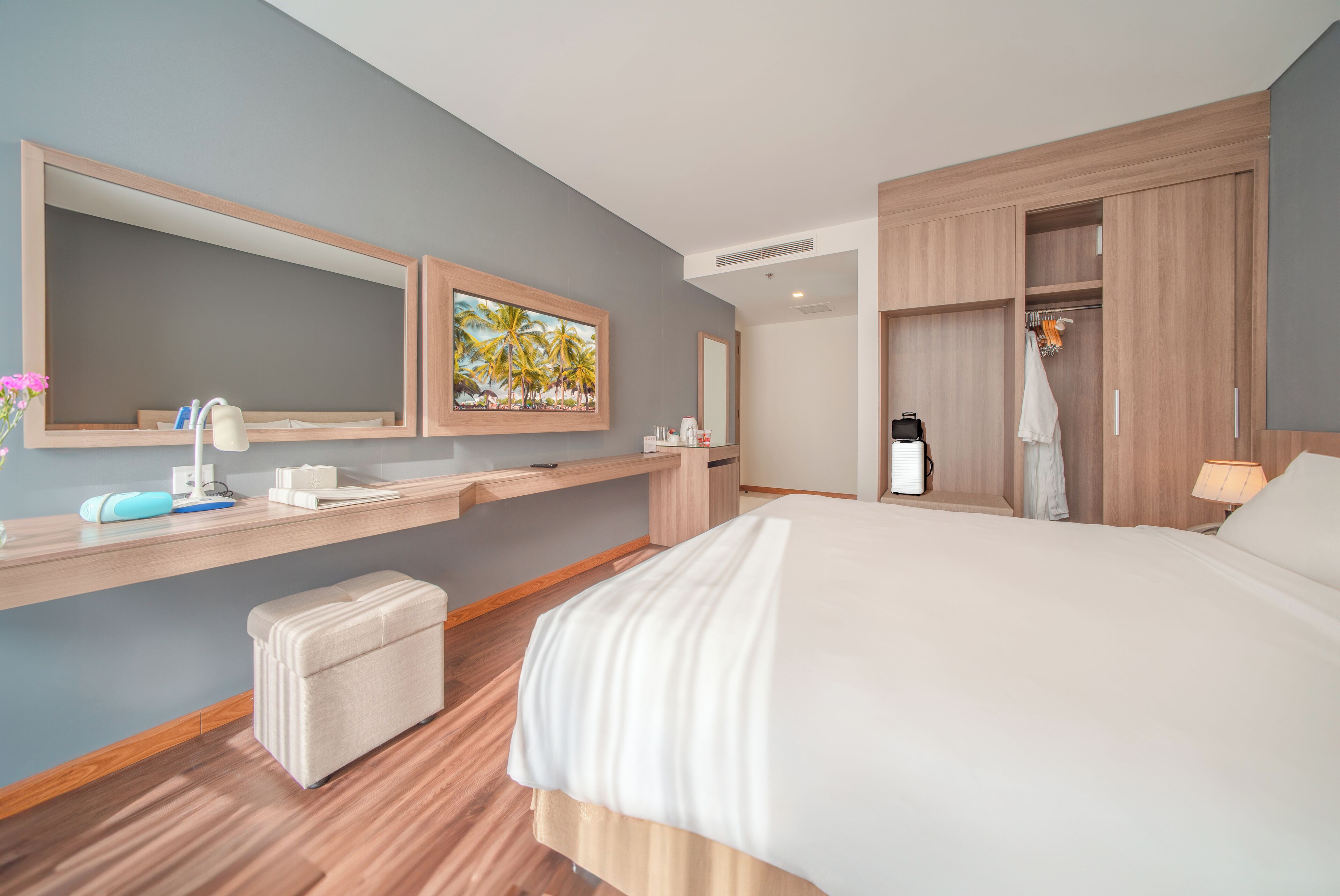 Quarto de hotel moderno com uma cama grande, uma toucador com espelho, um pequeno espaço de estar e um guarda-roupa.