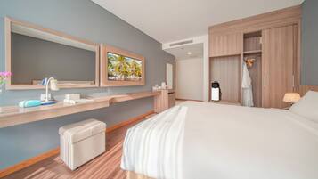 Quarto de hotel moderno com uma cama grande, uma toucador com espelho, um pequeno espaço de estar e um guarda-roupa.