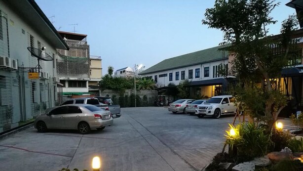 Uma área de estacionamento com vários carros, um edifício com varanda e um jardim bem iluminado.