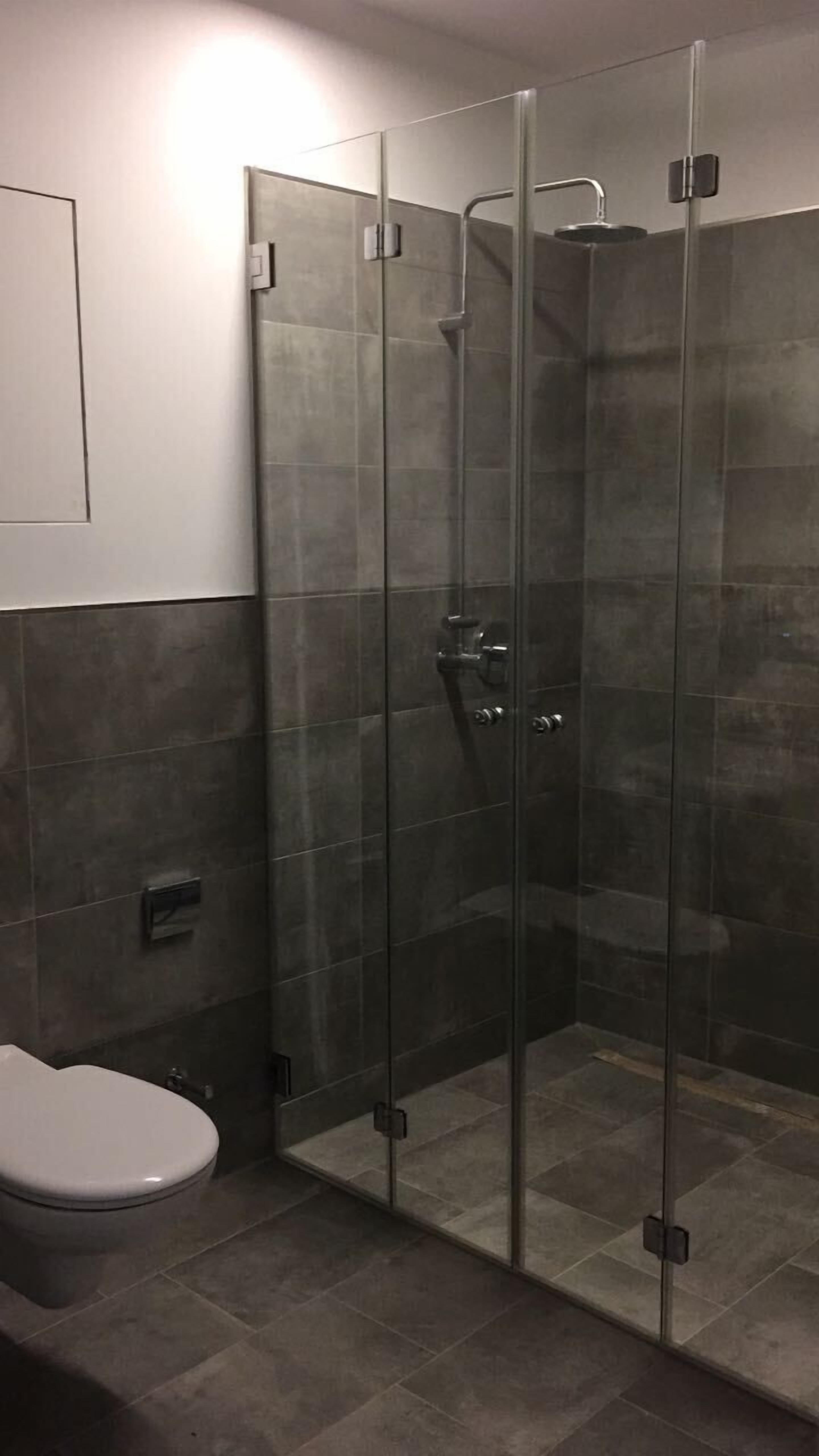 Uma casa de banho moderna com chuveiro em cabine de vidro, sanita e dispensador de toalhas fixado na parede.