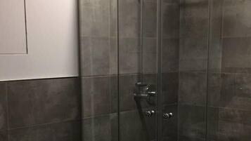 Uma casa de banho moderna com chuveiro em cabine de vidro, sanita e dispensador de toalhas fixado na parede.