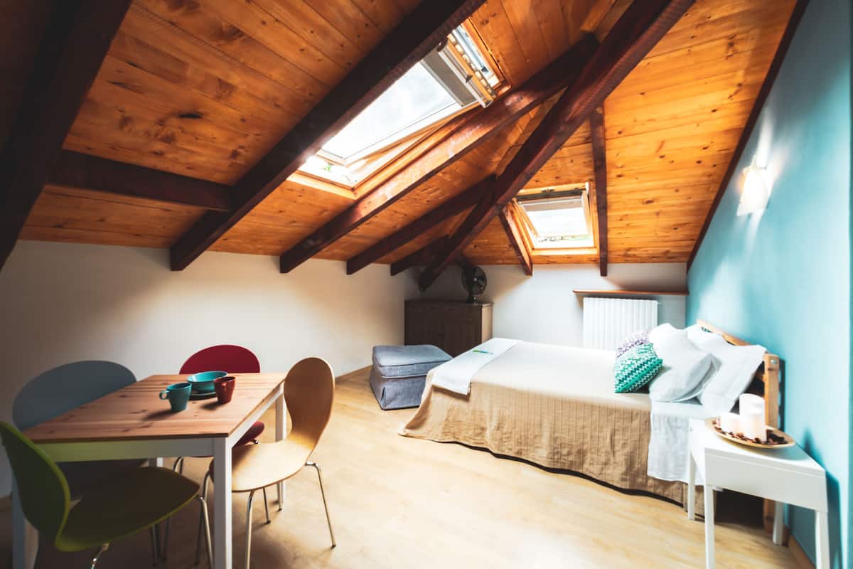 Um quarto de sótão acolhedor, com teto de madeira, uma cama, uma mesinha e uma cadeira.