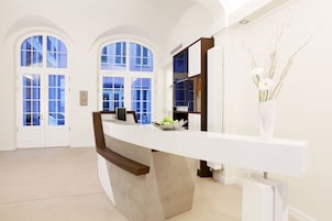 Uma área de recepção com um balcão branco curvo, uma grande janela em arco e um vaso com plantas secas.