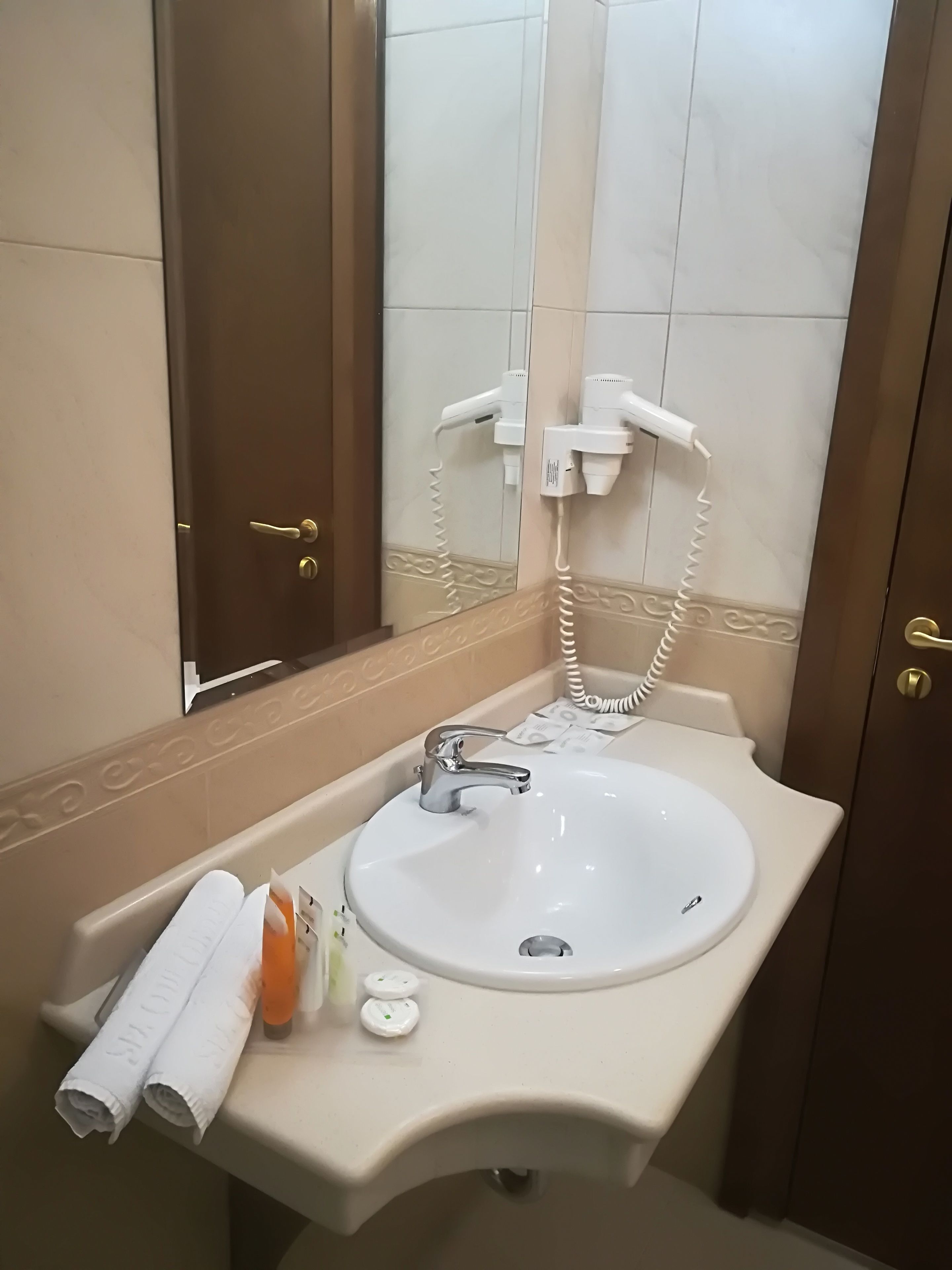 Casa de banho com lavatório branco, espelho e secador de cabelo.