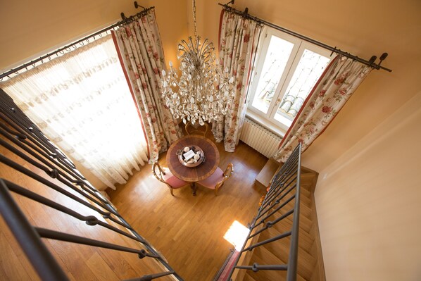 Uma escadaria leva a uma sala de jantar com um candelabro, cortinas e piso de madeira.