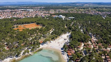 Vista aérea de uma cidade costeira com praia, áreas residenciais e um campo esportivo.