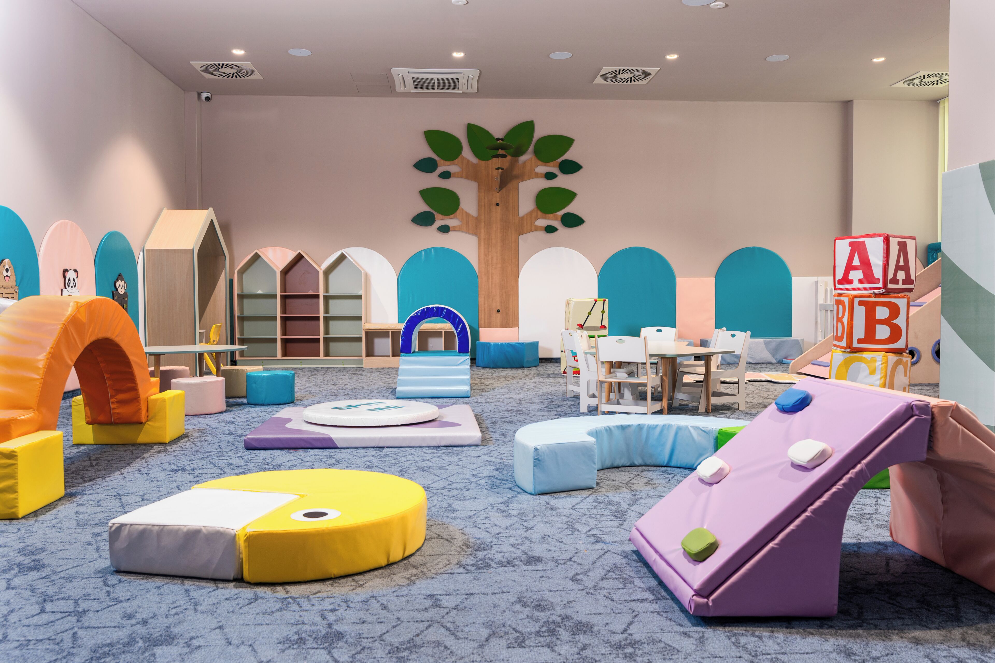 Uma área de recreação infantil com estruturas de brinquedo macio, uma mesa e cadeiras.
