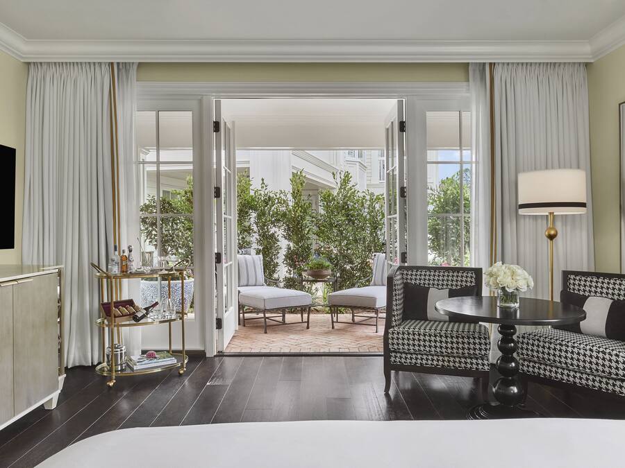 Quarto de hotel com cama, sofá, duas cadeiras, uma mesinha, televisão e vista para o exterior.