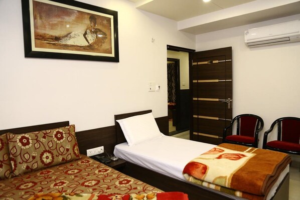 Quarto de hotel com uma cama, duas cadeiras, um quadro na parede e um ar condicionado.