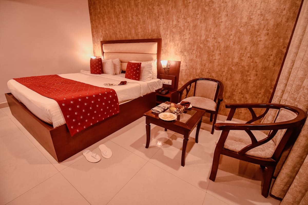 Quarto de hotel com cama, mesa de cabeceira, cadeira e uma pequena mesa com um prato e um copo.