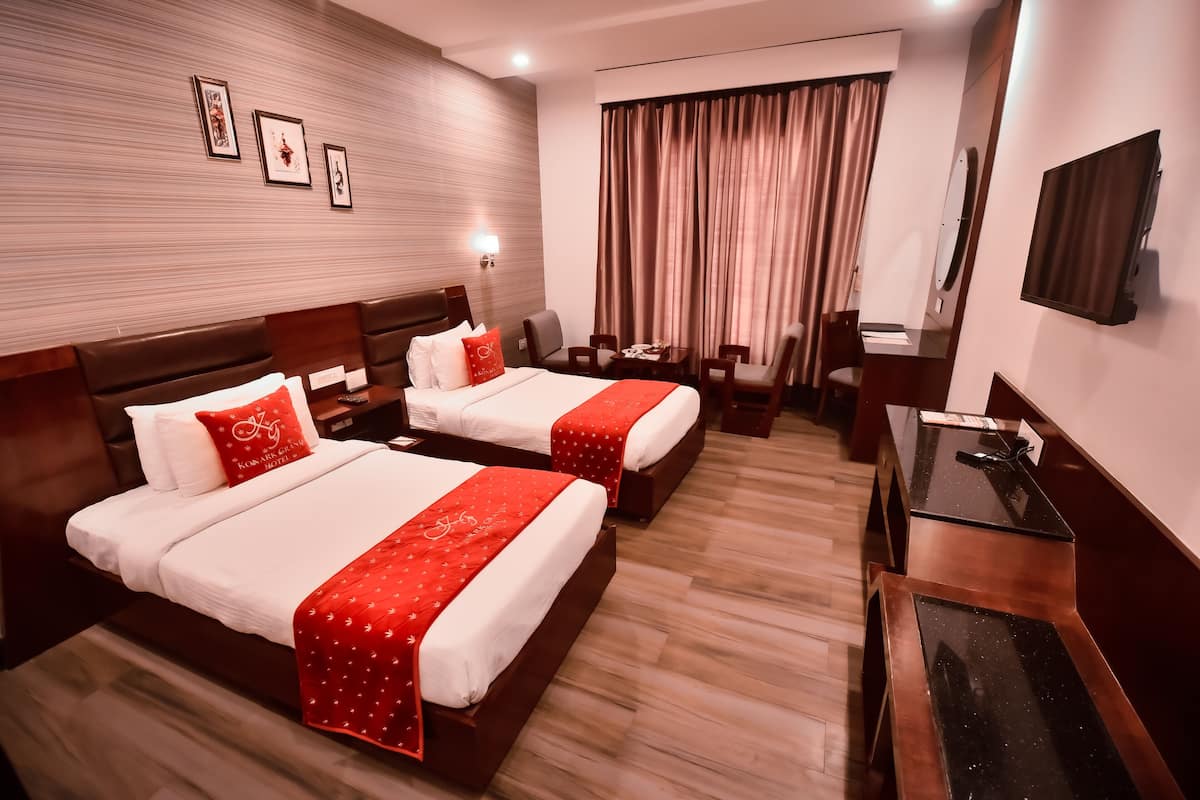 Quarto de hotel com duas camas, uma mesa, uma cadeira e uma televisão.