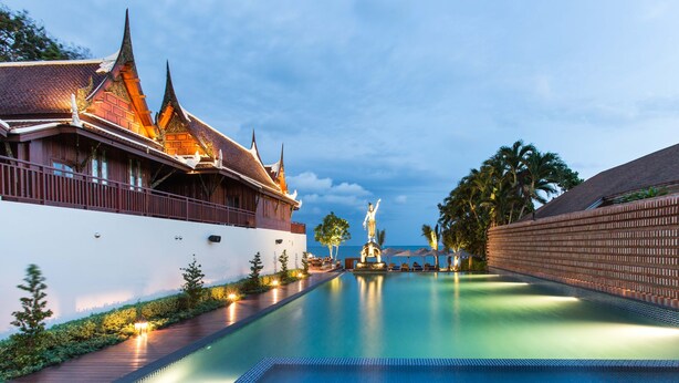 Piscina com um edifício em estilo arquitetônico tailandês tradicional de um lado e uma estrutura moderna do outro.
