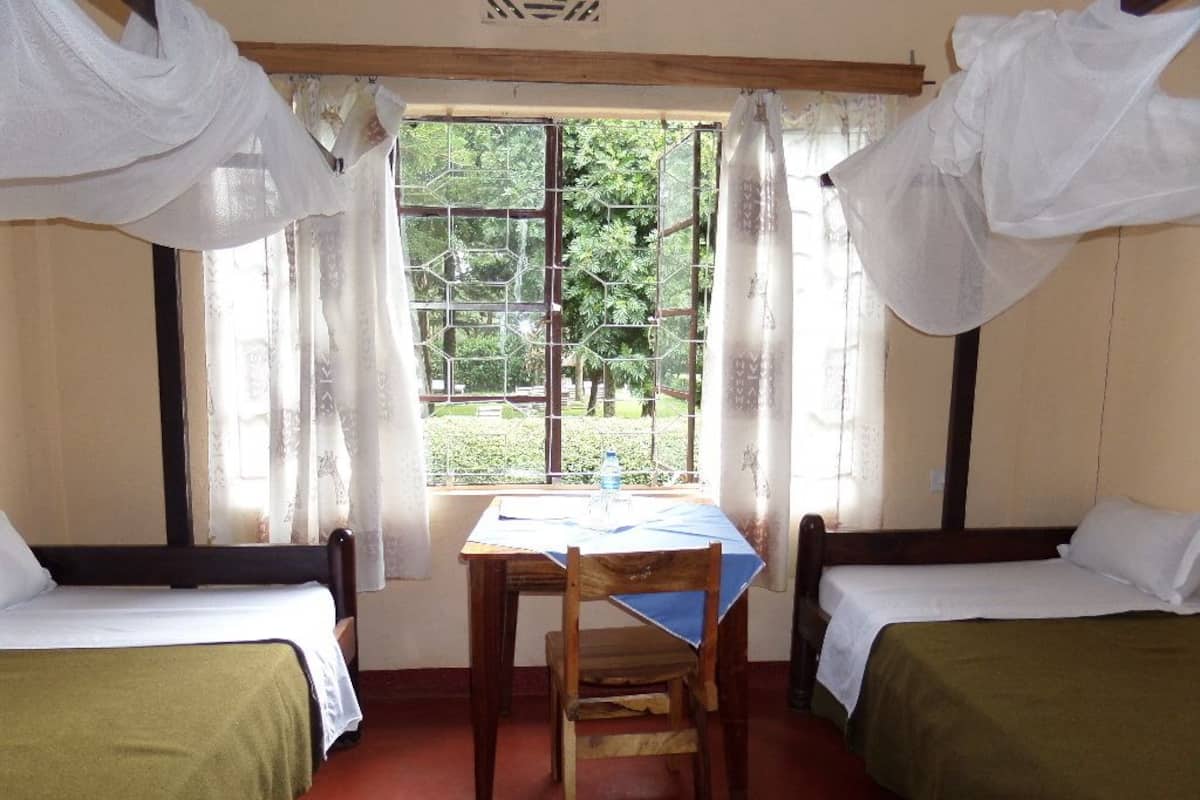 Quarto com duas camas, uma mesa e uma janela com cortinas.