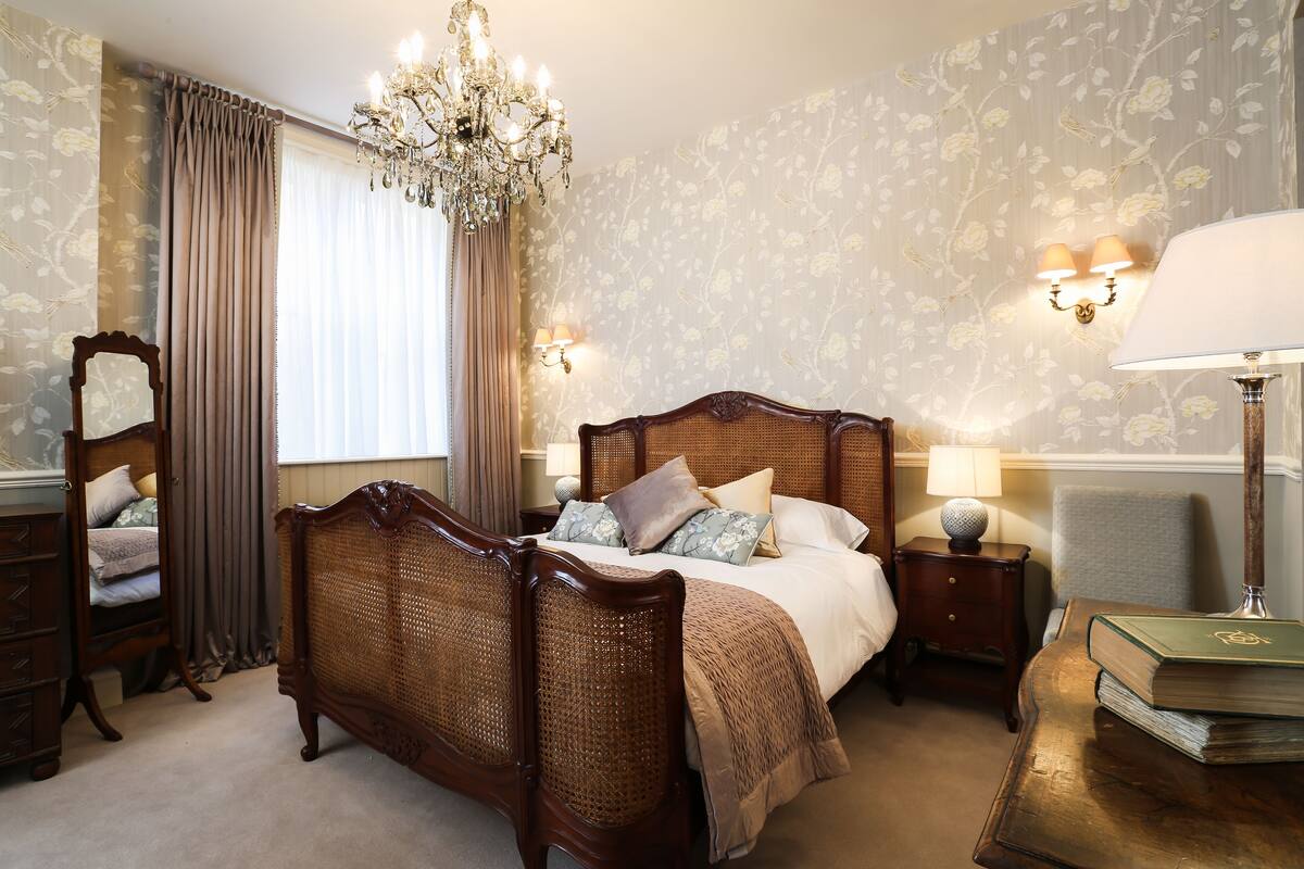 Quarto clássico com cama de dossel de madeira, um candelabro e papel de parede floral.