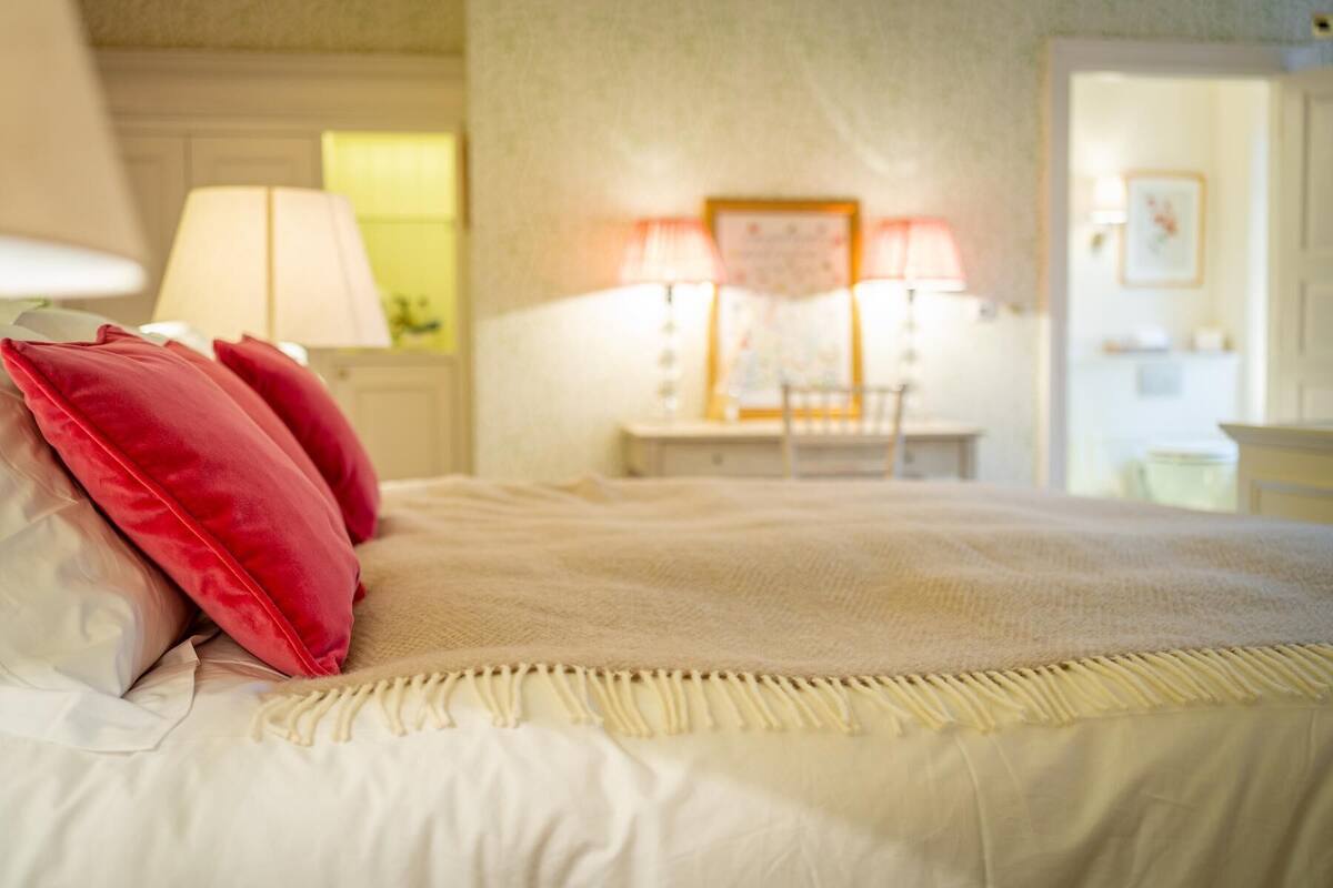 Cama com almofadas vermelhas, cobre branca e detalhe franjado.