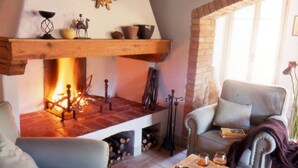 Uma sala de estar acolhedora com lareira, um sofá confortável, uma mesa de centro de madeira e uma estante de livros.