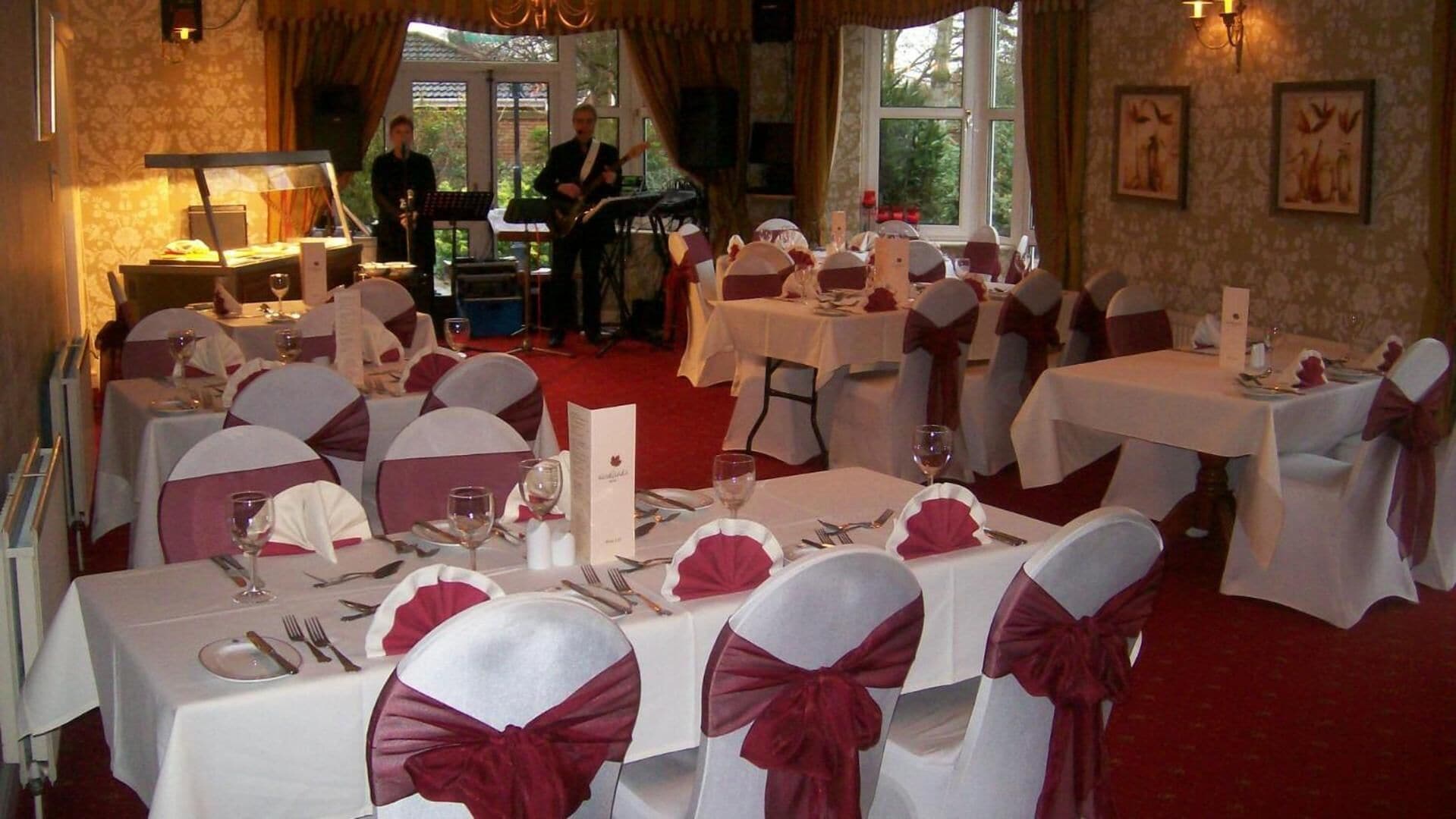 Uma sala de banquetes com mesas redondas dispostas para refeições, cada uma com toalhas brancas e fitas vermelhas.