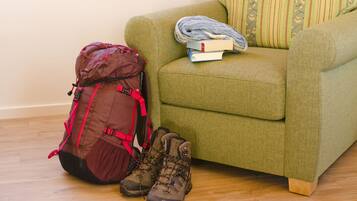 Um sofá verde com uma manta enrolada e um livro, uma mochila marrom e um par de botas de caminhada.