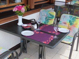 Mesa posta com pratos, talheres, saleiro e pimenteiro, um copo e um vaso com flores.