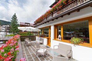 Um pátio de hotel com móveis de vime, janelas amplas e caixas de flores.