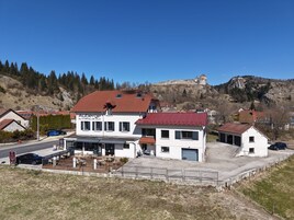 Um hotel com telhado vermelho, mesas ao ar livre e vista para uma colina com um castelo.