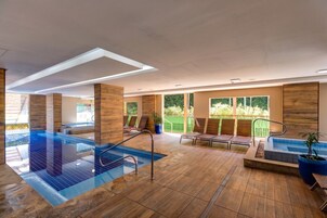Piscina interior moderna com água cristalina, piso de madeira e espreguiçadeiras.