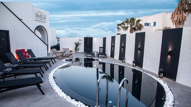 Área de piscina de hotel com espreguiçadeiras, uma mesinha e uma placa com a inscrição 'DIVELIA HOTEL'.