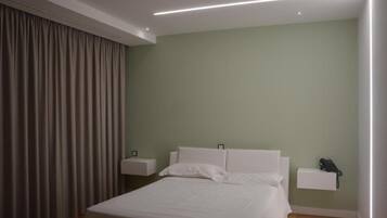 Quarto de hotel com uma cama, mesas de cabeceira, telefone e cortina.
