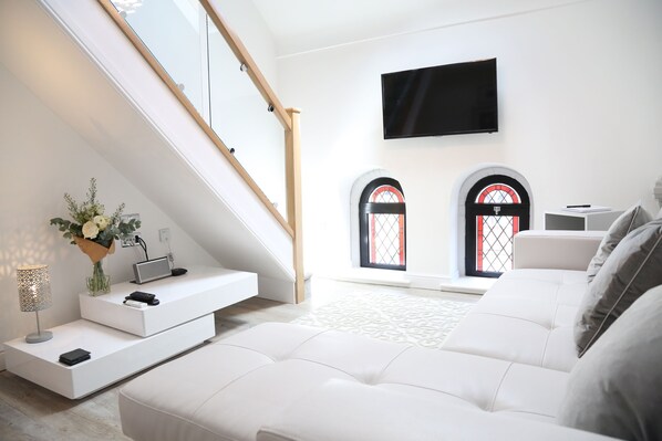 Uma sala de estar moderna com um sofá branco, uma TV de tela plana na parede e uma escada com corrimão de madeira.