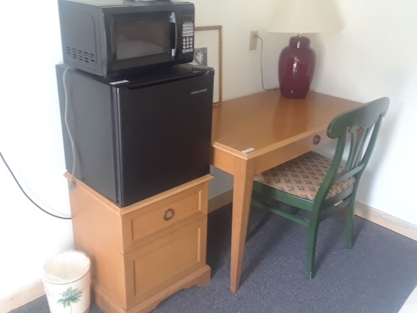 Uma pequena cozinha compacta com micro-ondas, geladeira e uma mesa de madeira com uma cadeira.