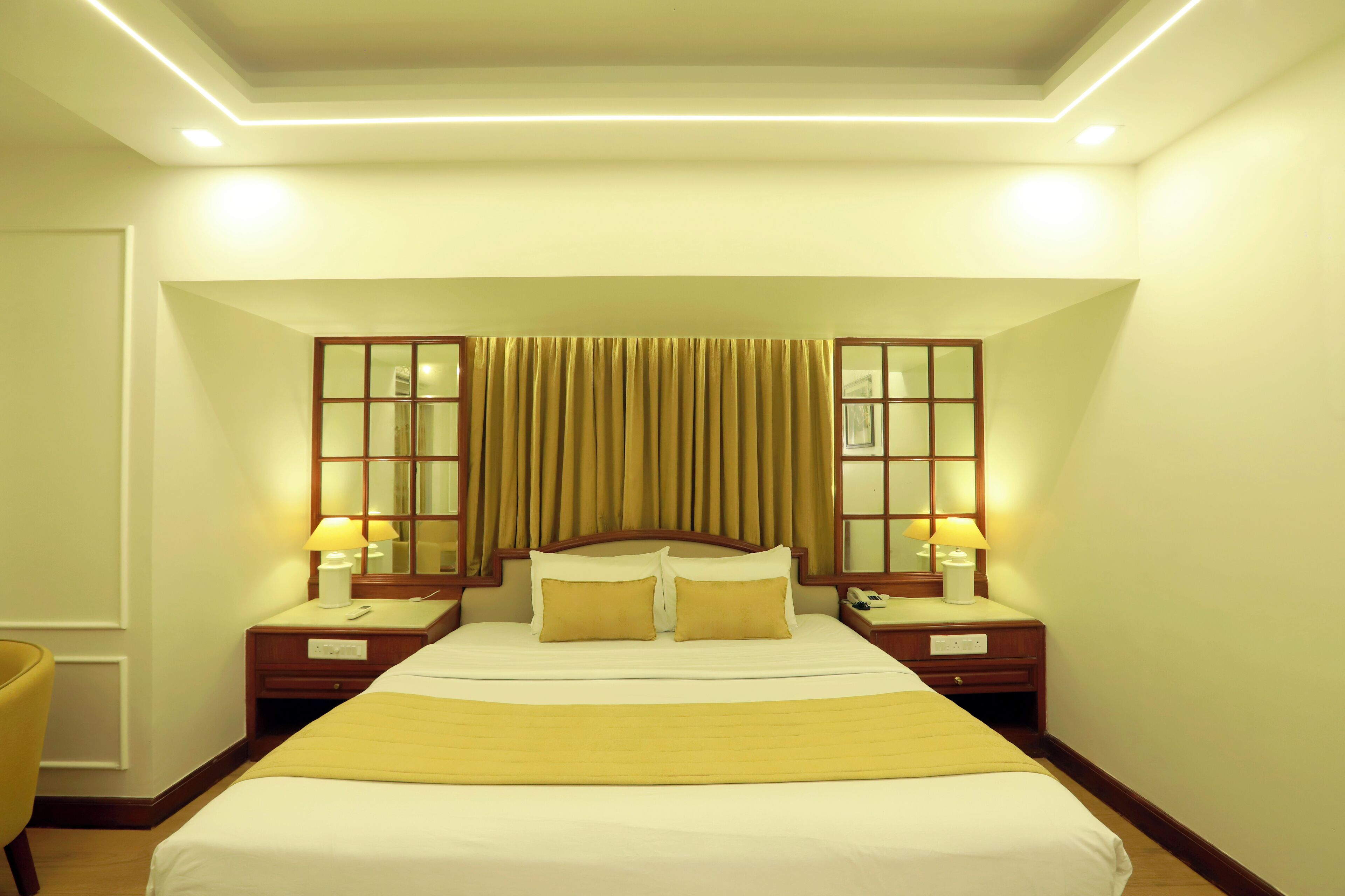 Quarto de hotel com uma cama grande, duas mesas de cabeceira com abajures, uma cadeira e uma janela com cortinas.