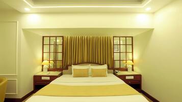 Quarto de hotel com uma cama grande, duas mesas de cabeceira com abajures, uma cadeira e uma janela com cortinas.