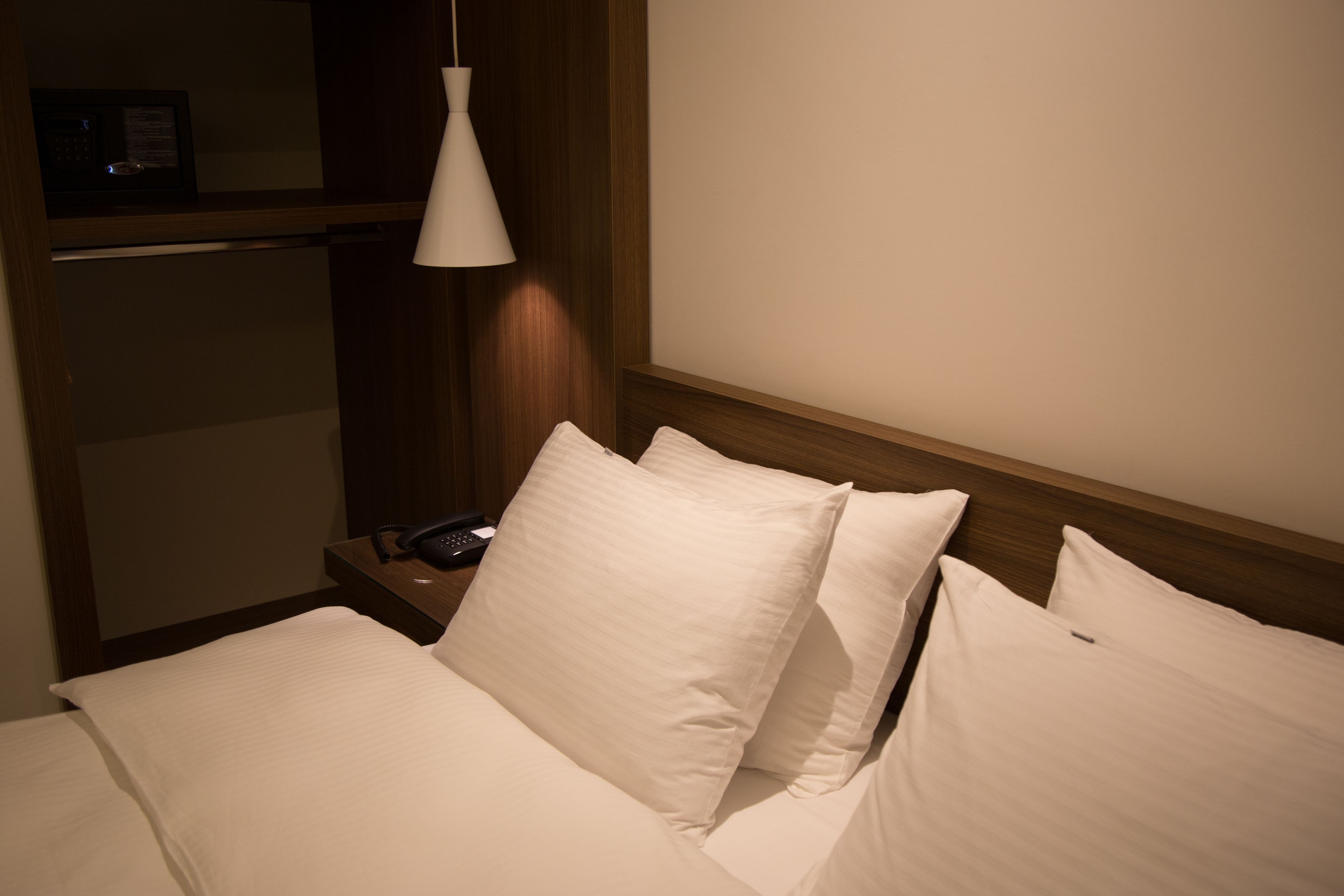 Cama bem arrumada com lençóis brancos, mesa de cabeceira com abajur e micro-ondas em cima.