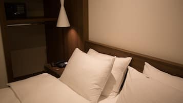Cama bem arrumada com lençóis brancos, mesa de cabeceira com abajur e micro-ondas em cima.