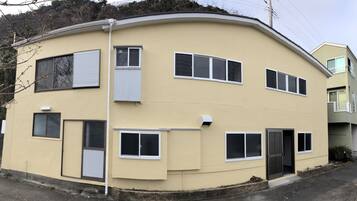 Um edifício de dois andares com várias janelas, uma porta de garagem e uma pequena construção anexa.